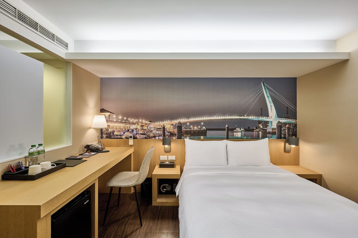 Quarto de hotel com cama, escrivaninha, cadeira e um mural da paisagem urbana na parede.