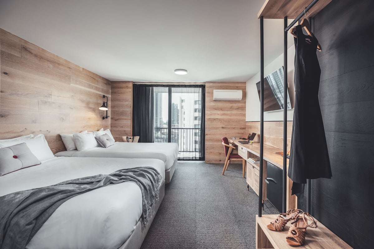 Quarto de hotel moderno com duas camas, uma escrivaninha e uma televisão.