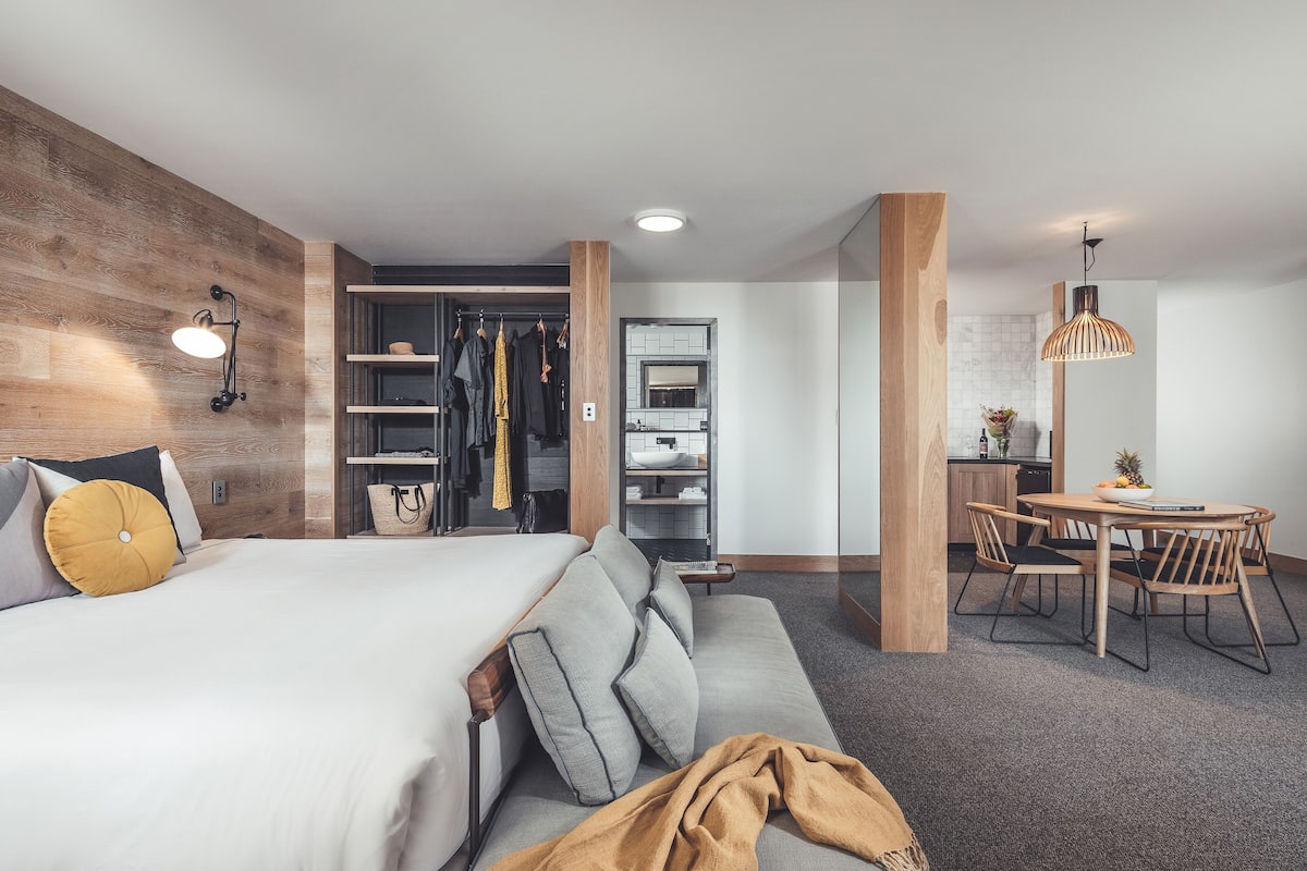 Quarto de hotel moderno com cama, sofá, área de refeições e armário.