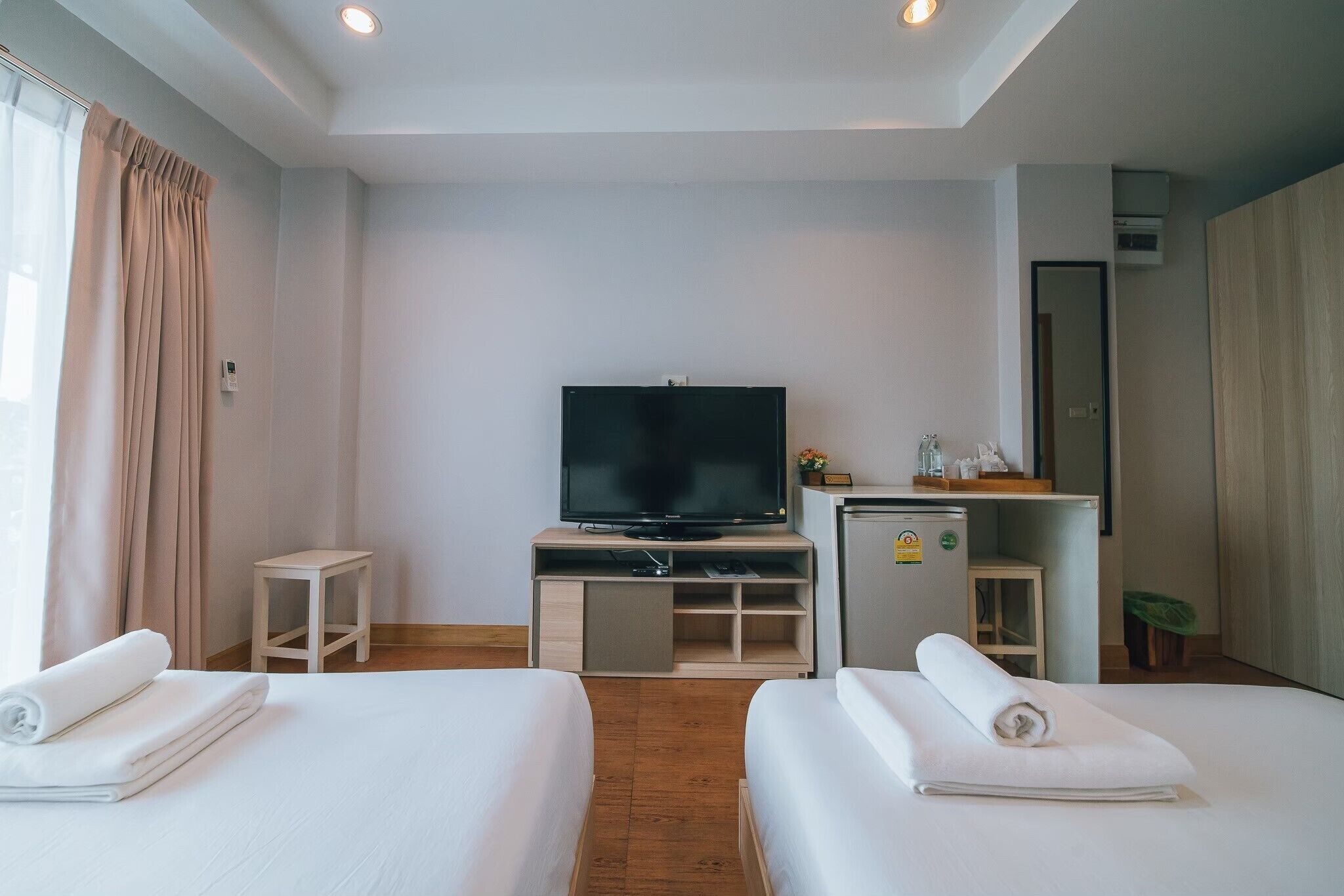 Quarto de hotel com duas camas, televisão, uma mesinha e frigobar.