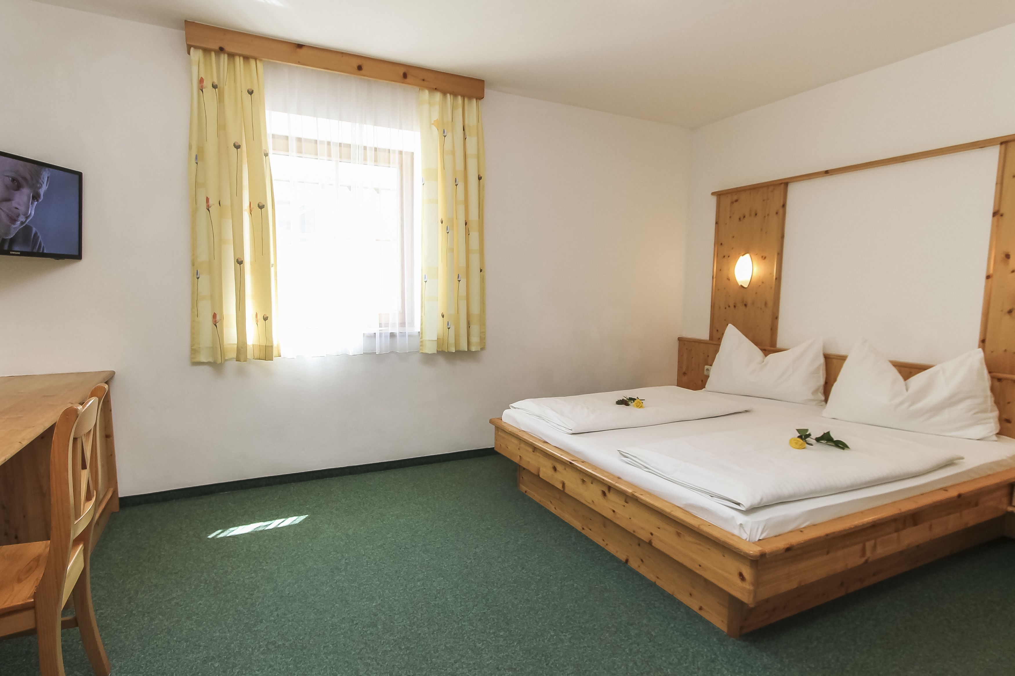 Quarto com cama de madeira, escrivaninha e televisão na parede.