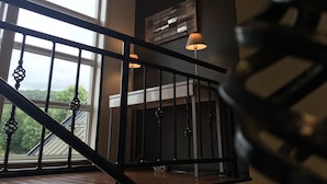 Uma escada com corrimão preto, vista para o exterior através de grandes janelas e uma luminária fixada na parede.