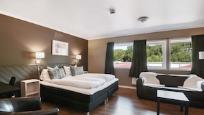 Quarto de hotel moderno com uma cama grande, um sofá, uma escrivaninha e uma janela com cortinas.