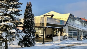 Um hotel moderno com fachada coberta de neve, grandes janelas e cerca branca de piquete.