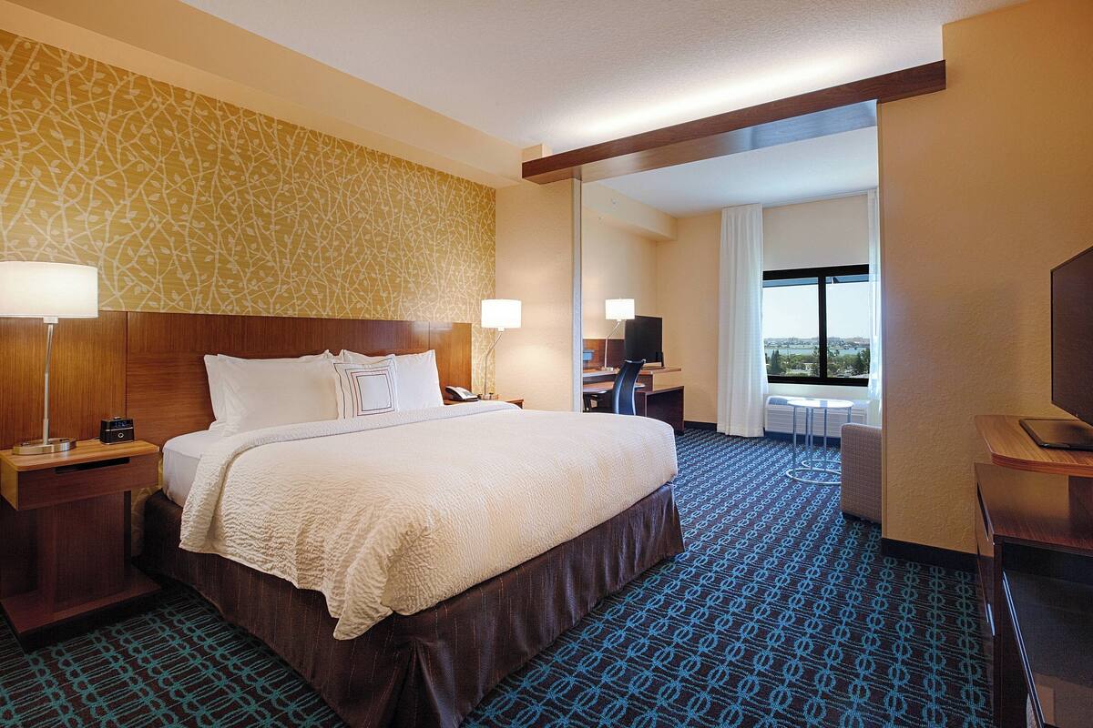 Quarto de hotel com uma cama grande, uma escrivaninha, uma televisão e vista para a cidade pela janela.