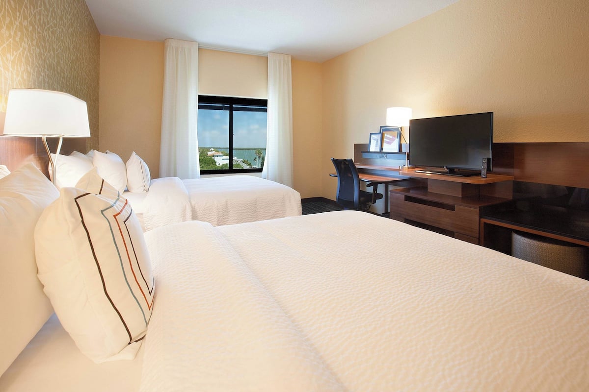 Quarto de hotel com duas camas, uma escrivaninha com televisão e uma janela com vista.