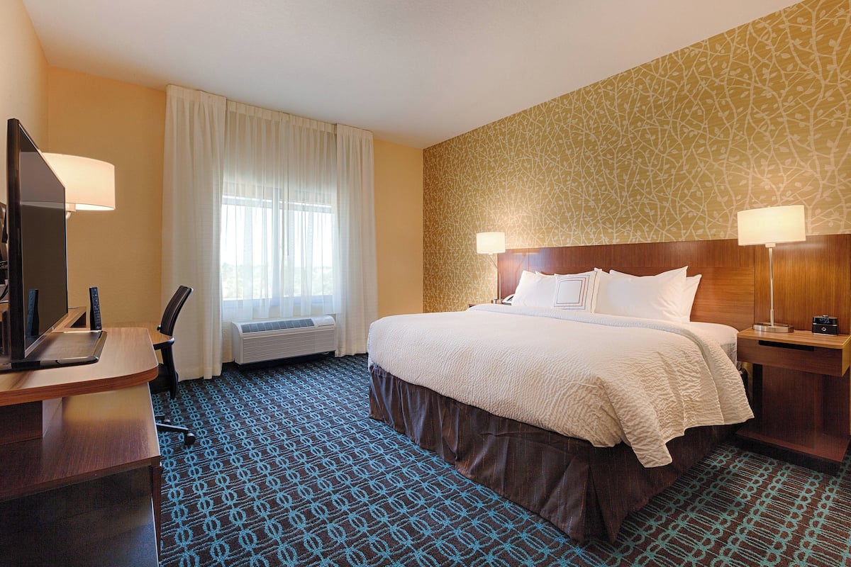 Quarto de hotel com cama, escrivaninha, cadeira e televisão.