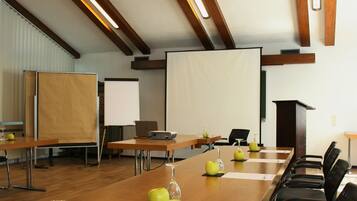 Uma sala de conferências com uma mesa comprida, cadeiras, uma tela de projetor e um púlpito.