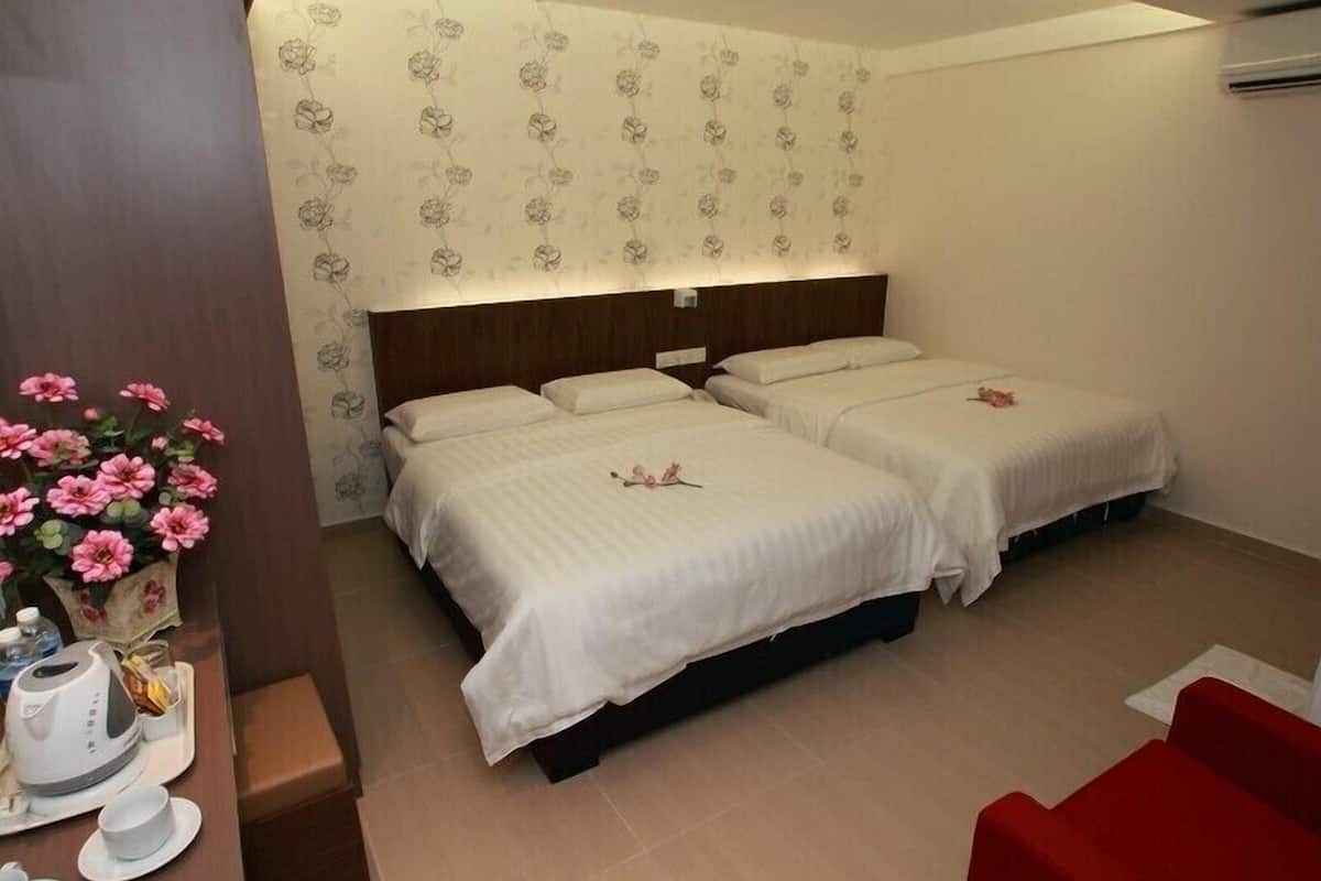 Quarto de hotel com duas camas, uma mesinha com chaleira e chávenas, e uma cadeira vermelha.
