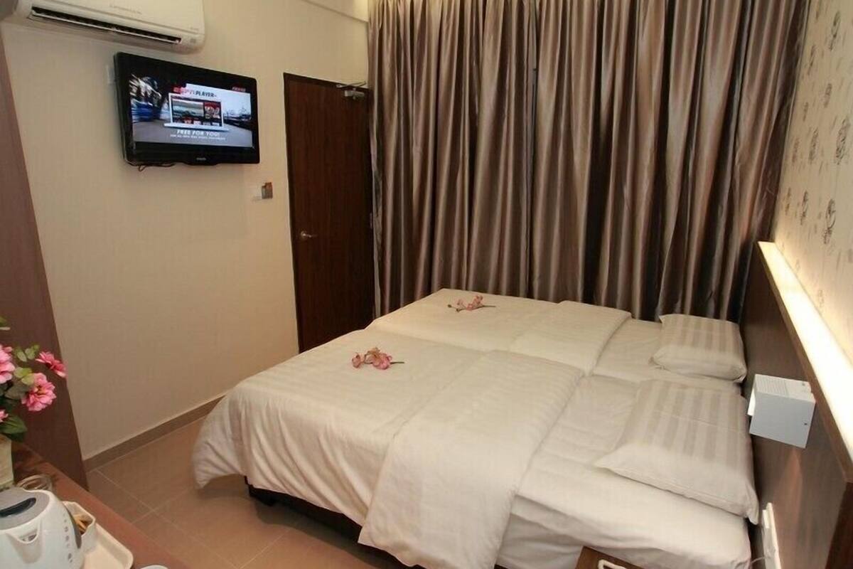 Quarto de hotel com cama, televisão na parede, cortina e pequena mesa com chaleira e xícaras.
