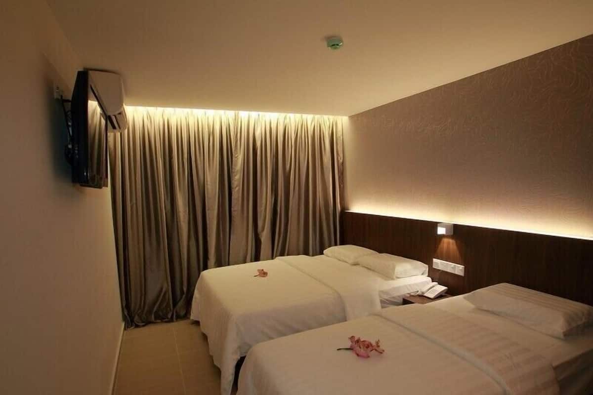 Quarto de hotel com duas camas, uma janela grande com cortinas, uma TV fixada na parede e uma mesa de cabeceira com abajur.