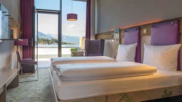 Quarto de hotel com cama, escrivaninha, cadeira e vista para montanhas pela janela.