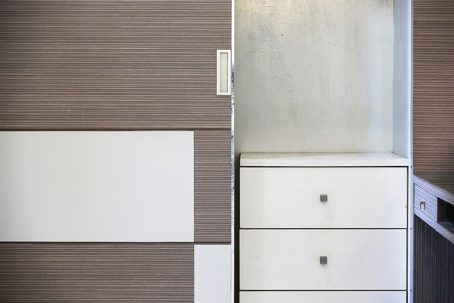 Um quarto com uma parede listrada, um armário branco com duas gavetas e uma pequena prateleira branca.
