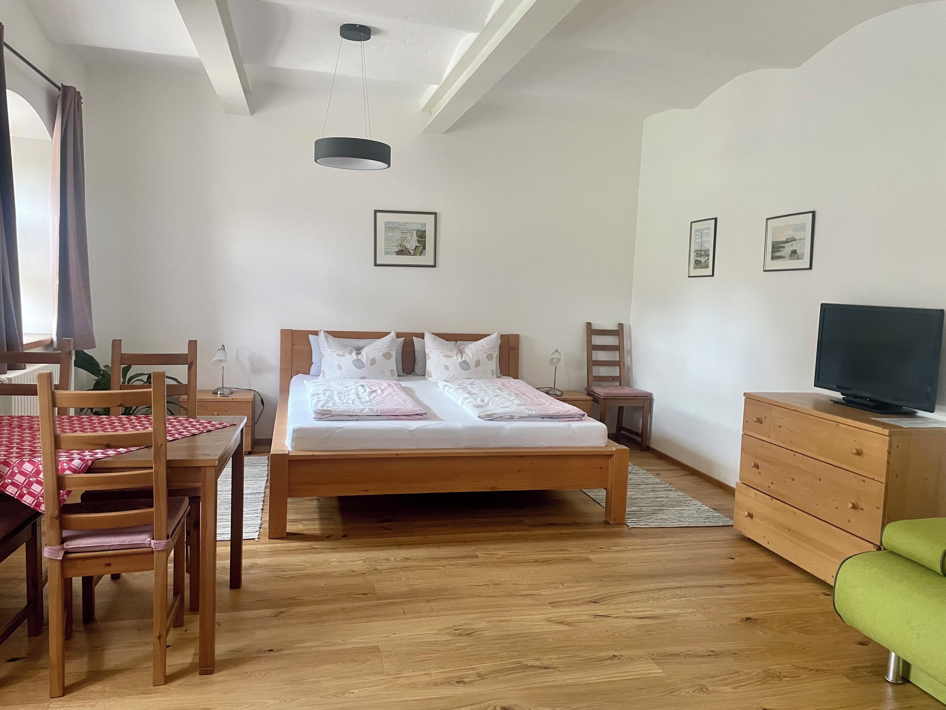 Quarto com cama de madeira, escrivaninha com cadeiras, televisão e quadros na parede.