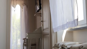 Um corredor estreito com piso de madeira, uma cama com almofadas, uma cadeira e um guarda-roupa.