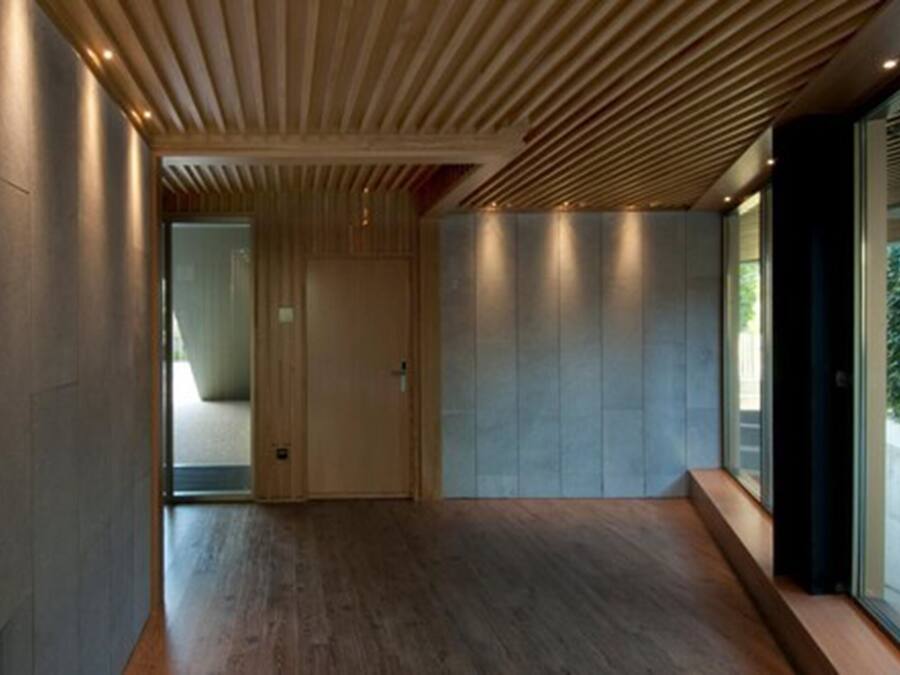 Corredor moderno com teto de ripas de madeira, piso de madeira e porta de vidro que dá para outro quarto.