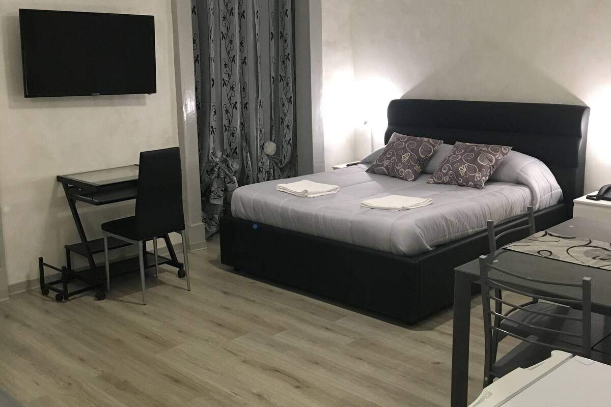 Quarto moderno com cama, escrivaninha, cadeira e televisão.