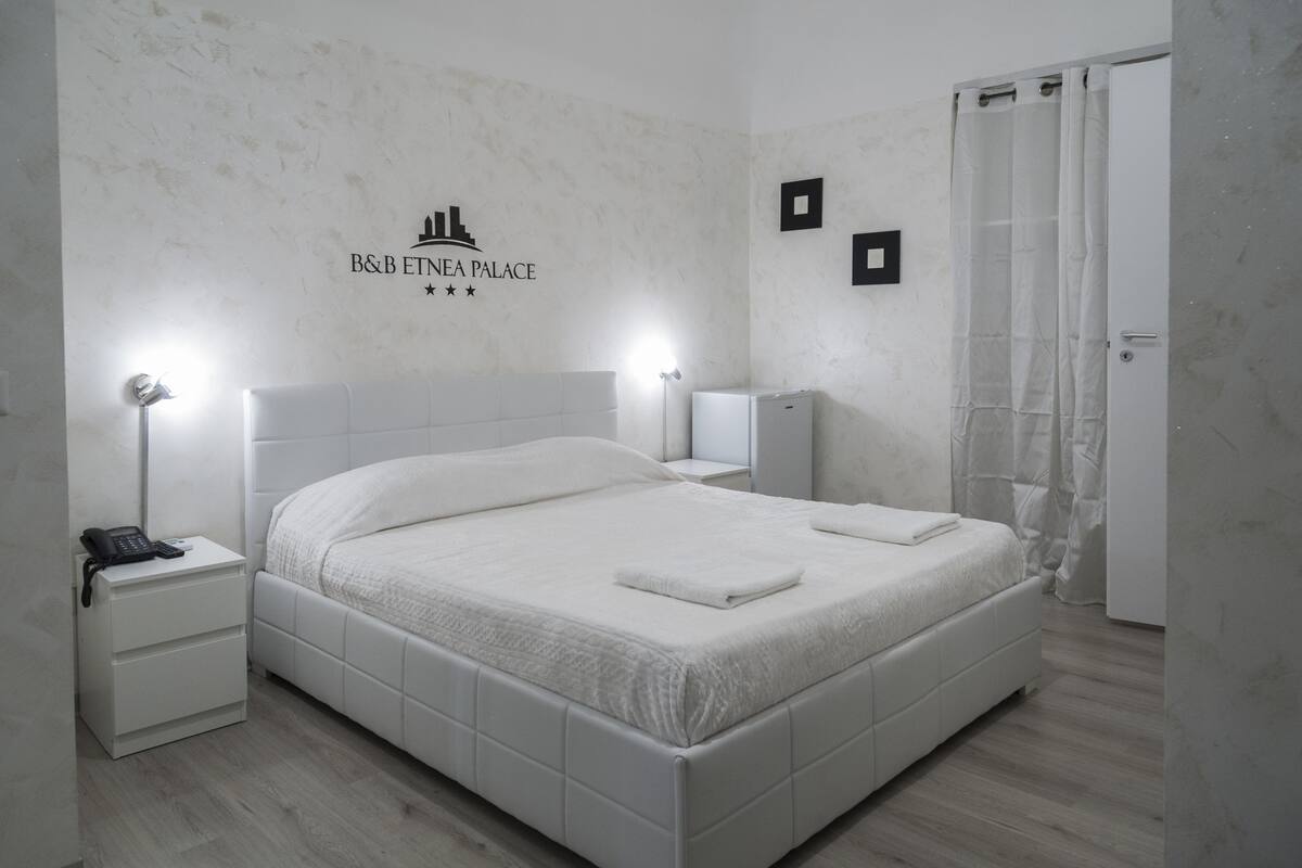 Quarto com cama, mesas de cabeceira, luminária na parede e cortina de chuveiro.