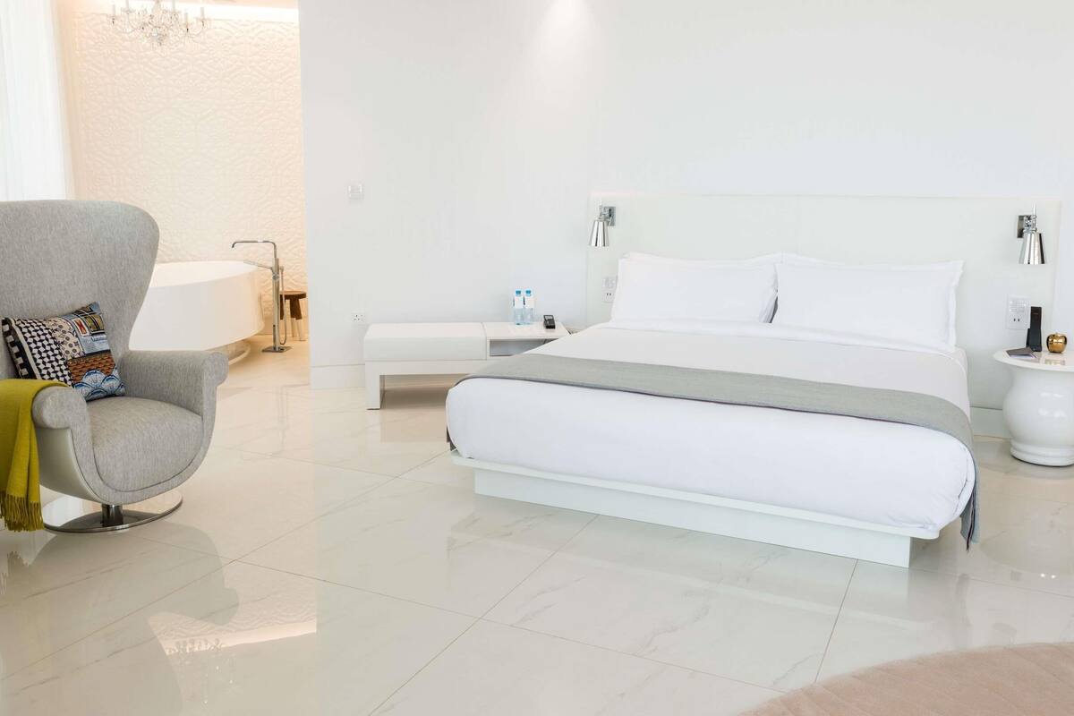 Um quarto moderno com uma cama grande, uma cadeira, uma mesa de cabeceira e um abajur.