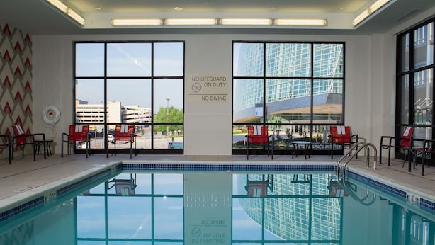 Piscina com salva-vidas, cadeiras e vista para um edifício moderno.