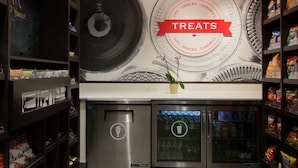 Loja com um letreiro 'Treats', prateleiras repletas de lanches e uma vitrine refrigerada.