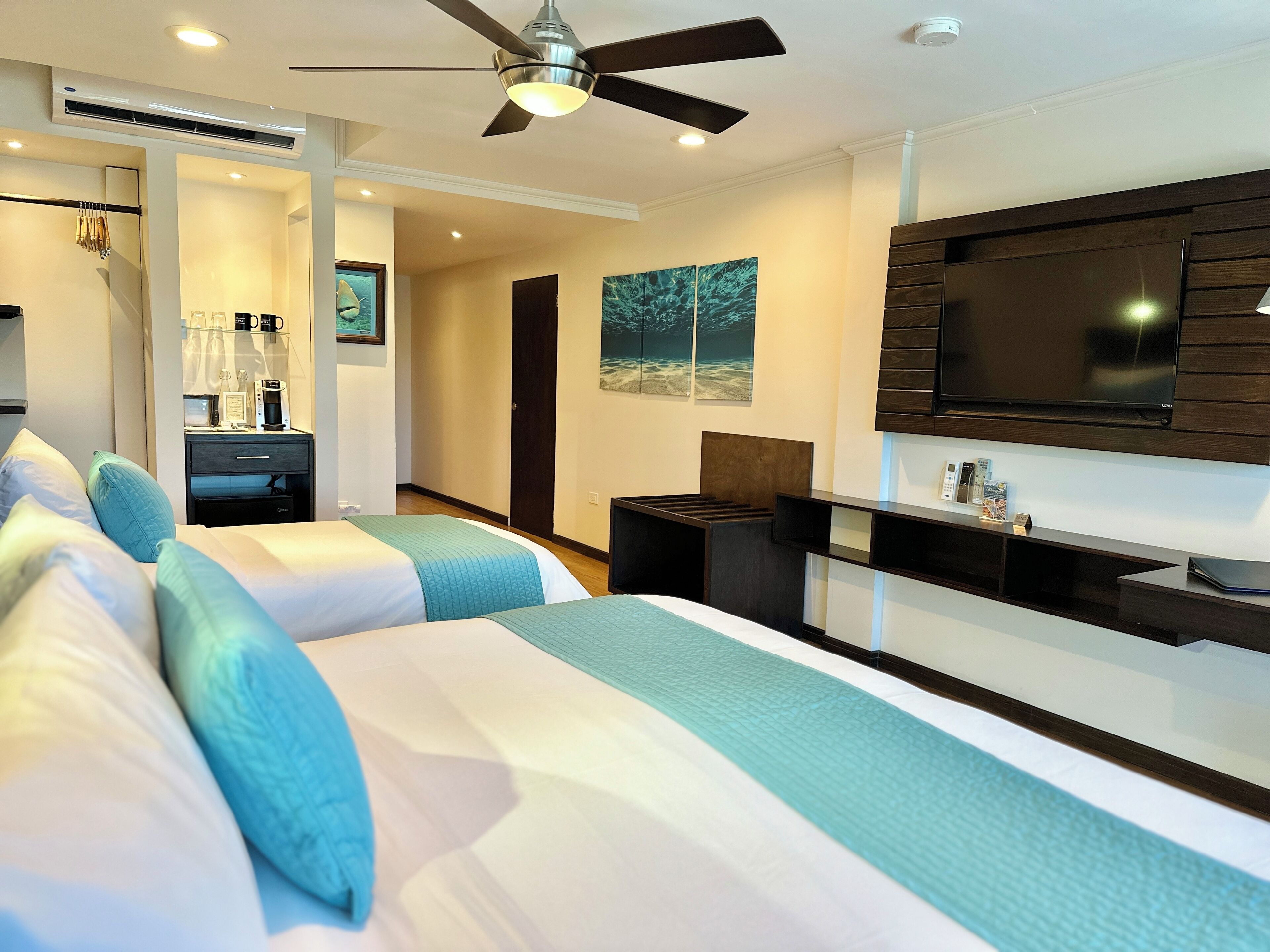 Quarto de hotel moderno com uma cama grande, TV fixada na parede, escrivaninha com cadeira e ventoinha no teto.