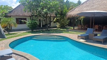 Piscina com escadas revestidas de azulejos, espreguiçadeiras e uma estrutura com telhado de palha.
