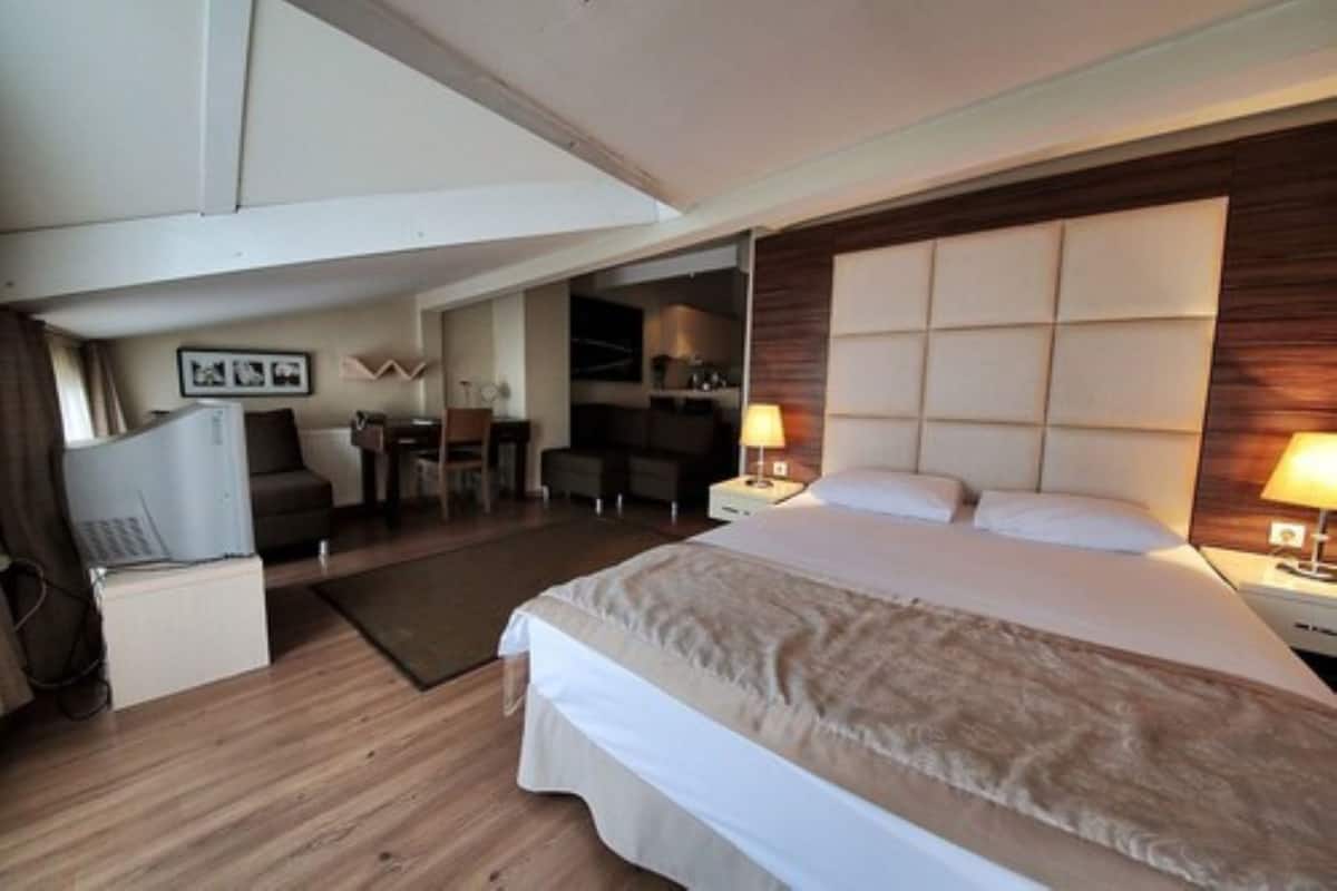 Quarto de hotel com uma cama grande, uma mesa, uma cadeira e uma pequena cozinha.