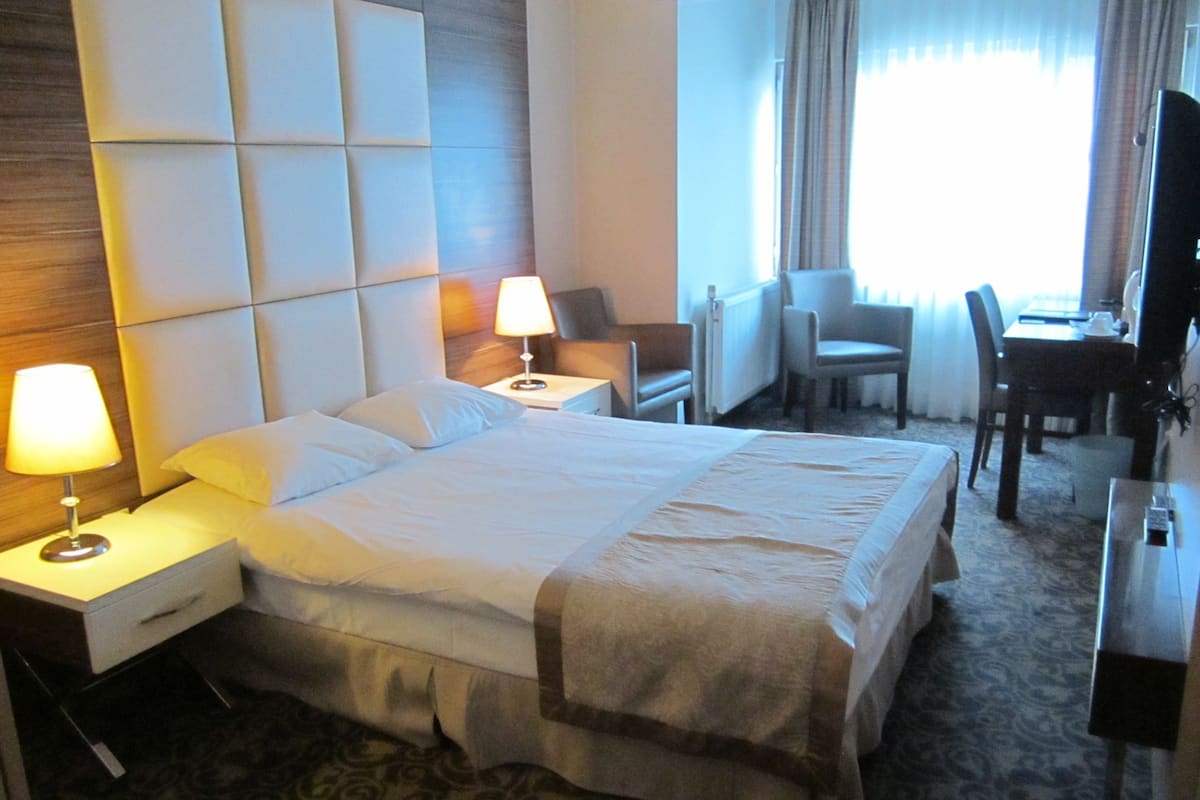 Quarto de hotel com uma cama grande, duas mesas de cabeceira com abajures, uma cadeira, uma escrivaninha e uma televisão.