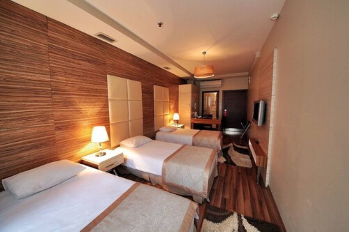 Quarto de hotel com três camas, painéis de madeira nas paredes, uma TV e um abajur na mesa de cabeceira.