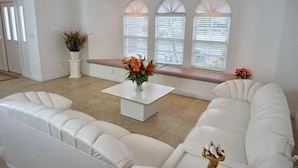 Uma sala de estar moderna com um sofá branco, uma mesa de centro branca e um banco com um arranjo de flores.