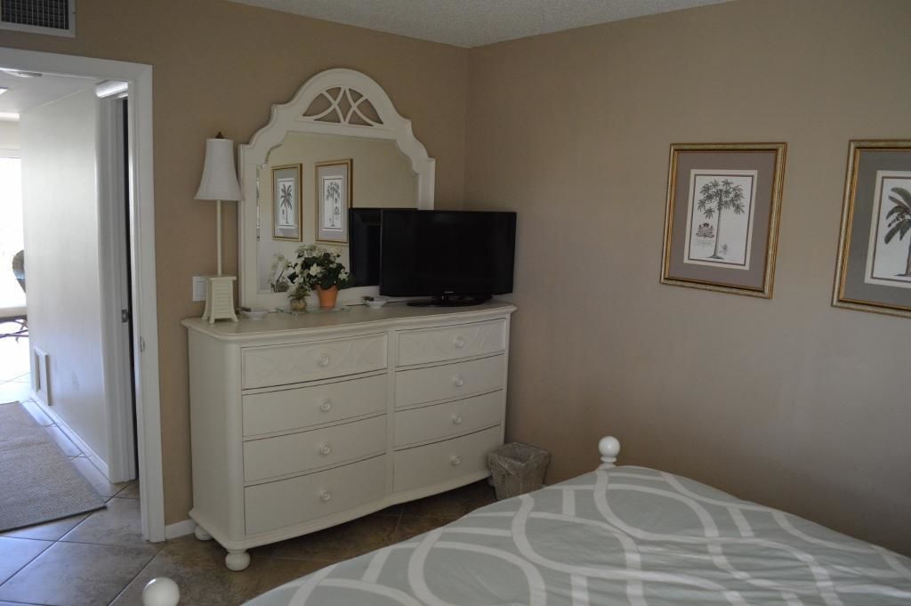Quarto com cama, cômoda, televisão e quadros nas paredes.
