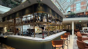 Uma área de bar moderna com balcão curvo, várias prateleiras com garrafas e um espaço de estar com cadeiras.