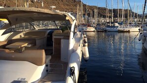 Marina com barcos atracados, um deck de madeira e montanhas ao fundo.
