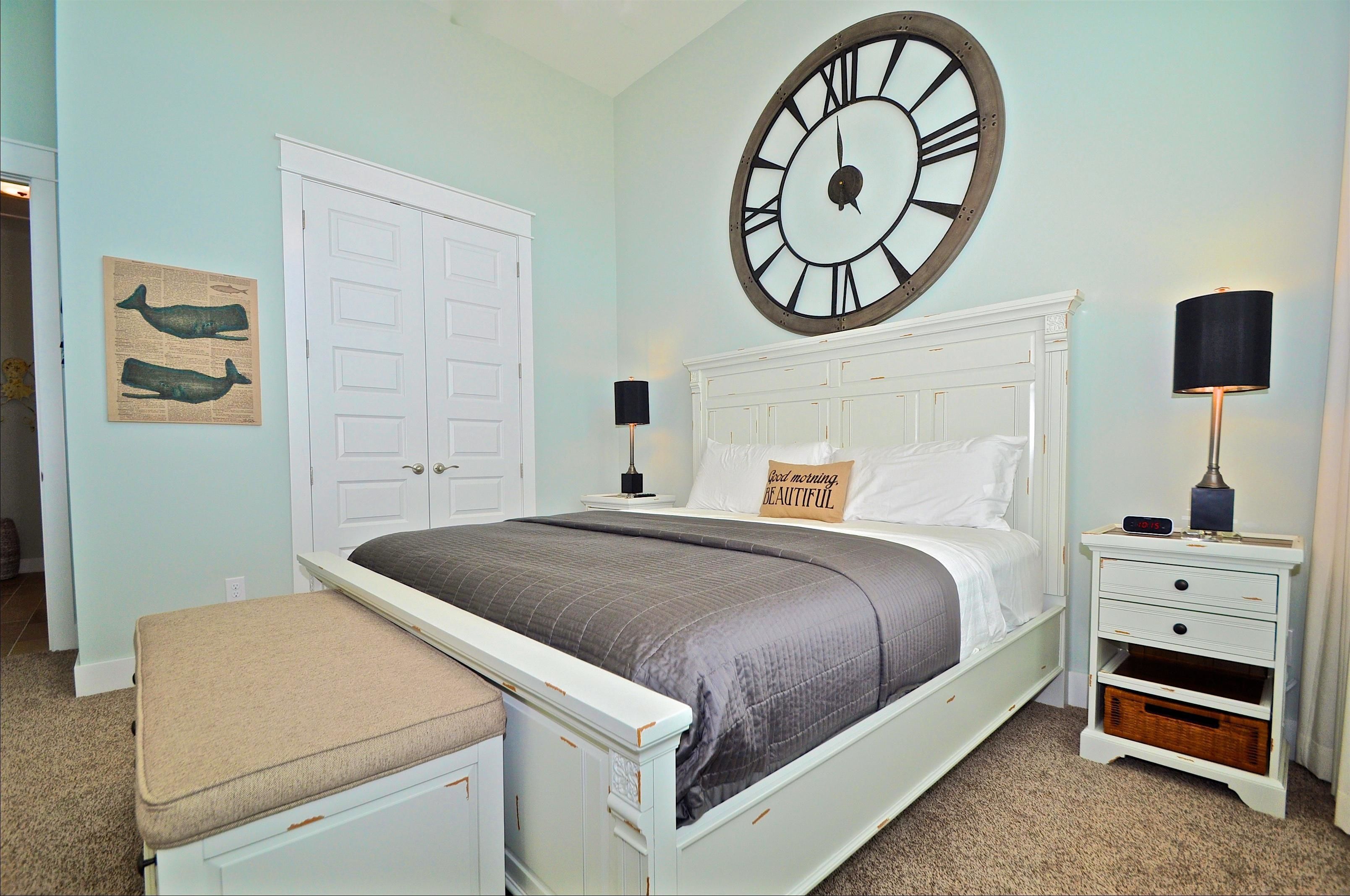 Quarto com cama, mesas de cabeceira, relógio e quadro na parede.