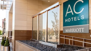 Entrada de um hotel Marriott, com uma placa grande, fachada de vidro e um vaso de pedra com pedriscos.
