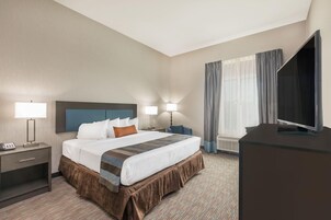 Quarto de hotel com cama, mesas de cabeceira, luminárias, televisão de tela plana e uma grande janela com cortinas.