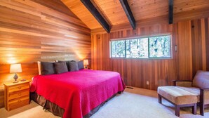 Quarto com painéis de madeira, uma cama, mesas de cabeceira, uma cadeira e uma janela.