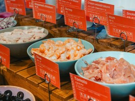 Buffet com tigelas identificadas de diversos frutos do mar e carnes.