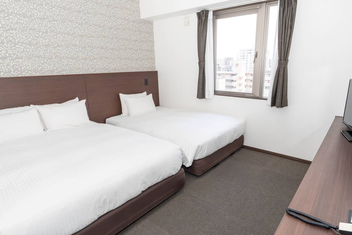 Quarto de hotel com duas camas, uma escrivaninha, uma televisão e uma janela com cortinas.