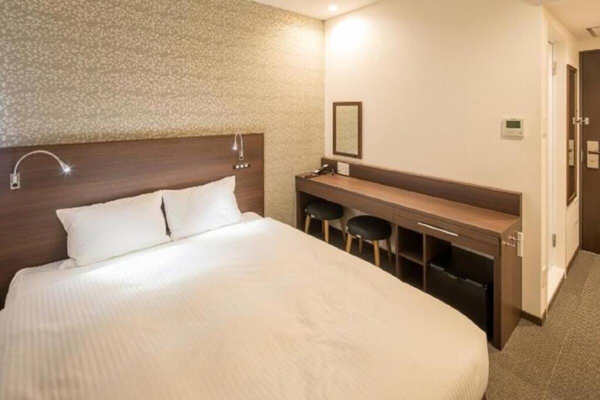 Quarto de hotel com uma cama grande, uma escrivaninha com espelho e um pequeno espaço para sentar.