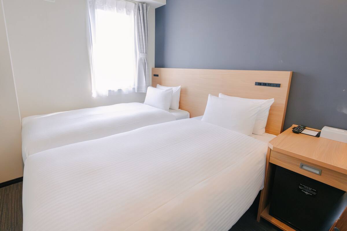 Quarto de hotel com duas camas, uma mesa de cabeceira com telefone e um pequeno armário.