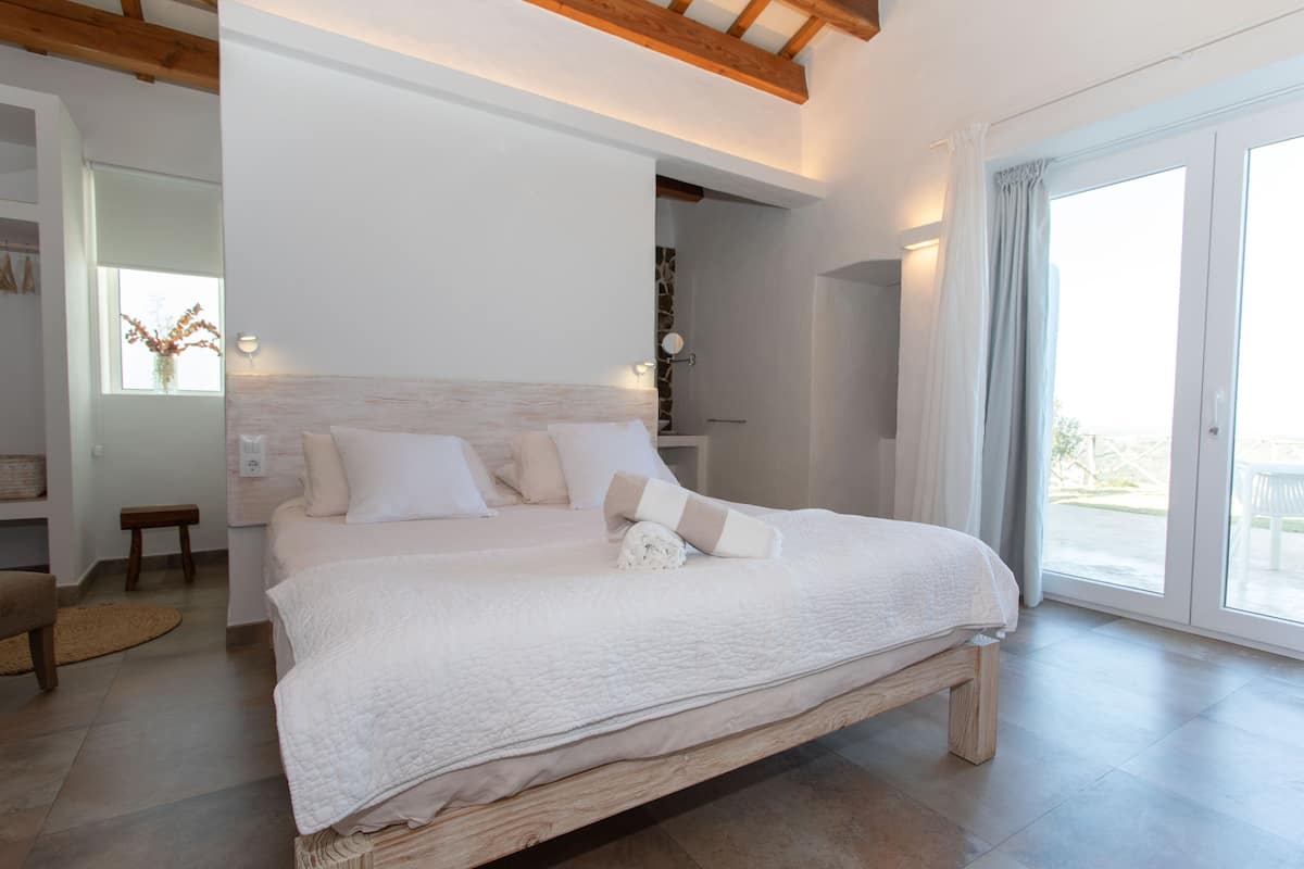 Quarto espaçoso com uma cama grande, cabeceira de madeira e vista através de uma porta de correr de vidro.