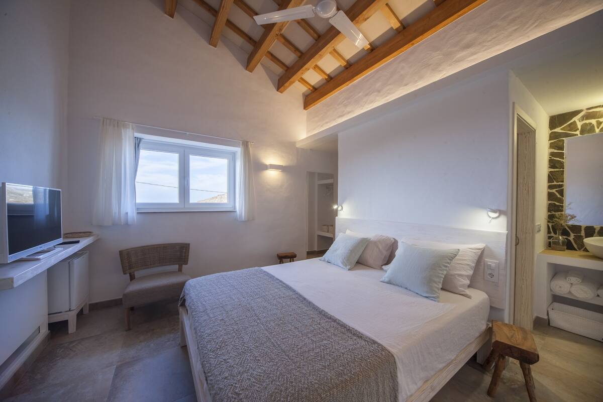 Quarto com cama, televisão, cadeira, mesa pequena e parede de pedra.