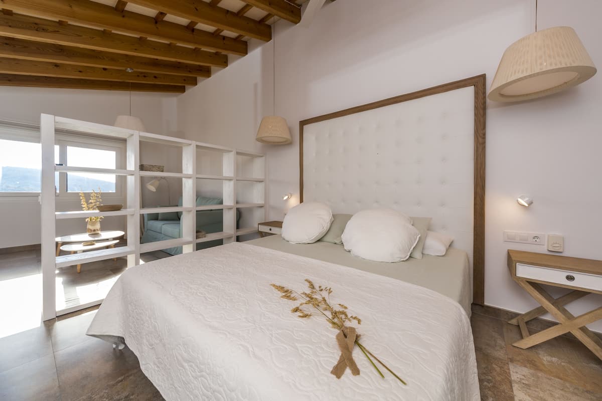 Quarto com uma cama grande, teto de madeira, cabeceira branca e mesa de cabeceira com abajur.