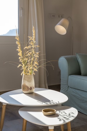 Um quarto com uma mesa redonda branca, um vaso com plantas secas, um sofá azul e um abajur.