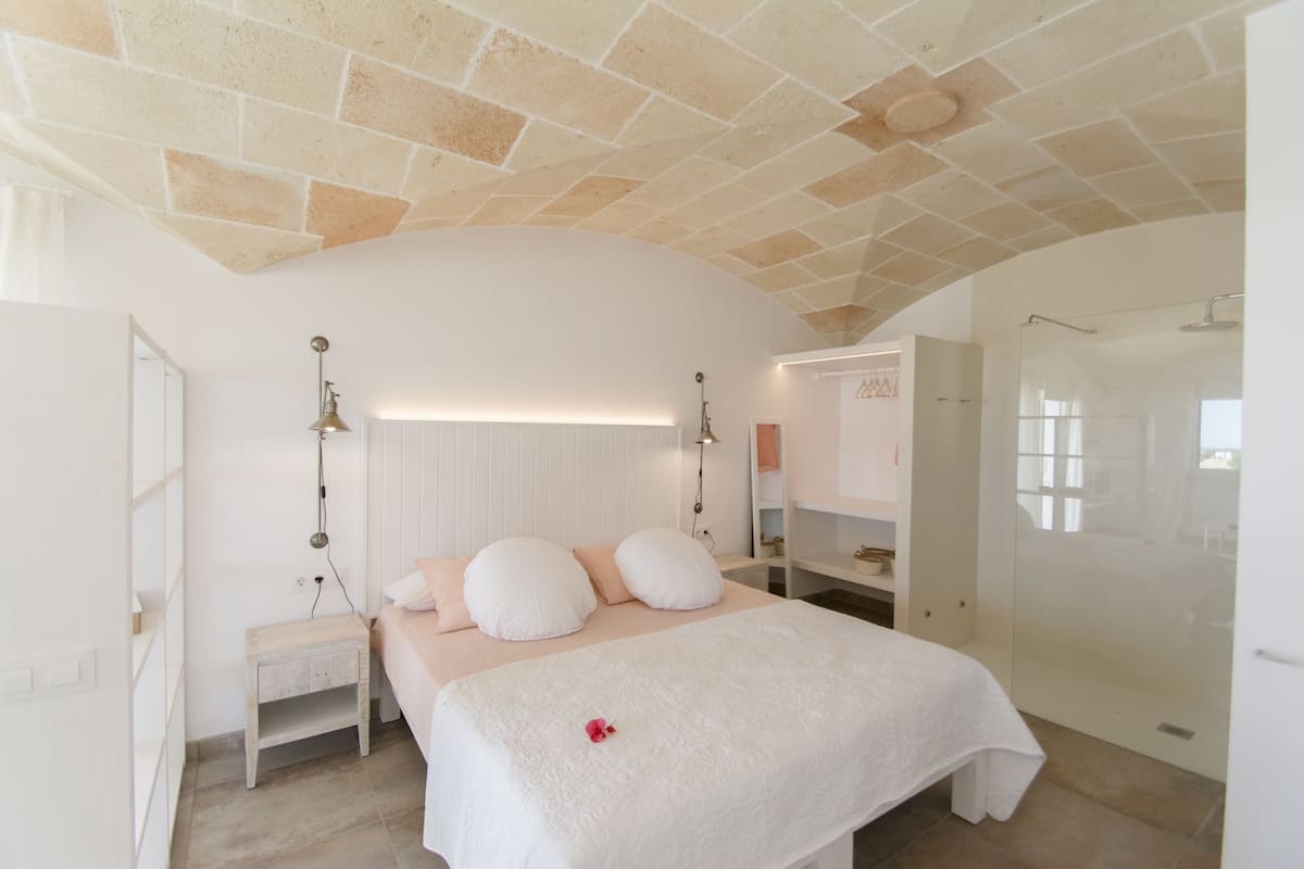 Quarto com cama grande, mesas de cabeceira, guarda-roupa e zona de duche.