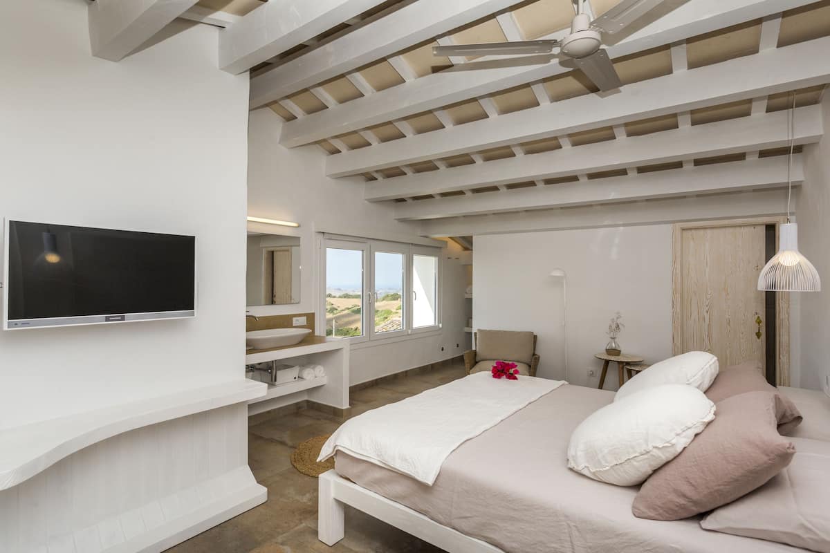 Quarto com cama, televisão, penteadeira e janela com vista.