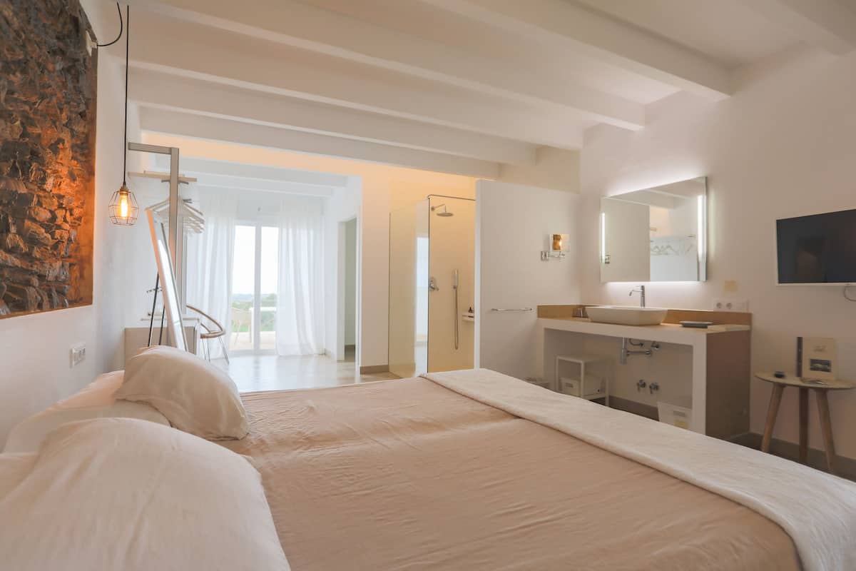 Quarto de hotel moderno com uma cama grande, banheiro com pia e espelho, e vista para o exterior.