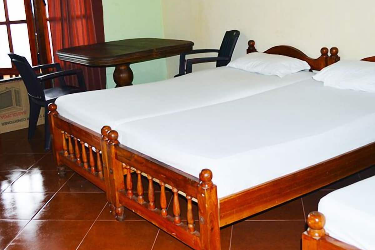 Uma cama de solteiro com estrutura de madeira e roupa de cama branca num quarto com chão de azulejos.